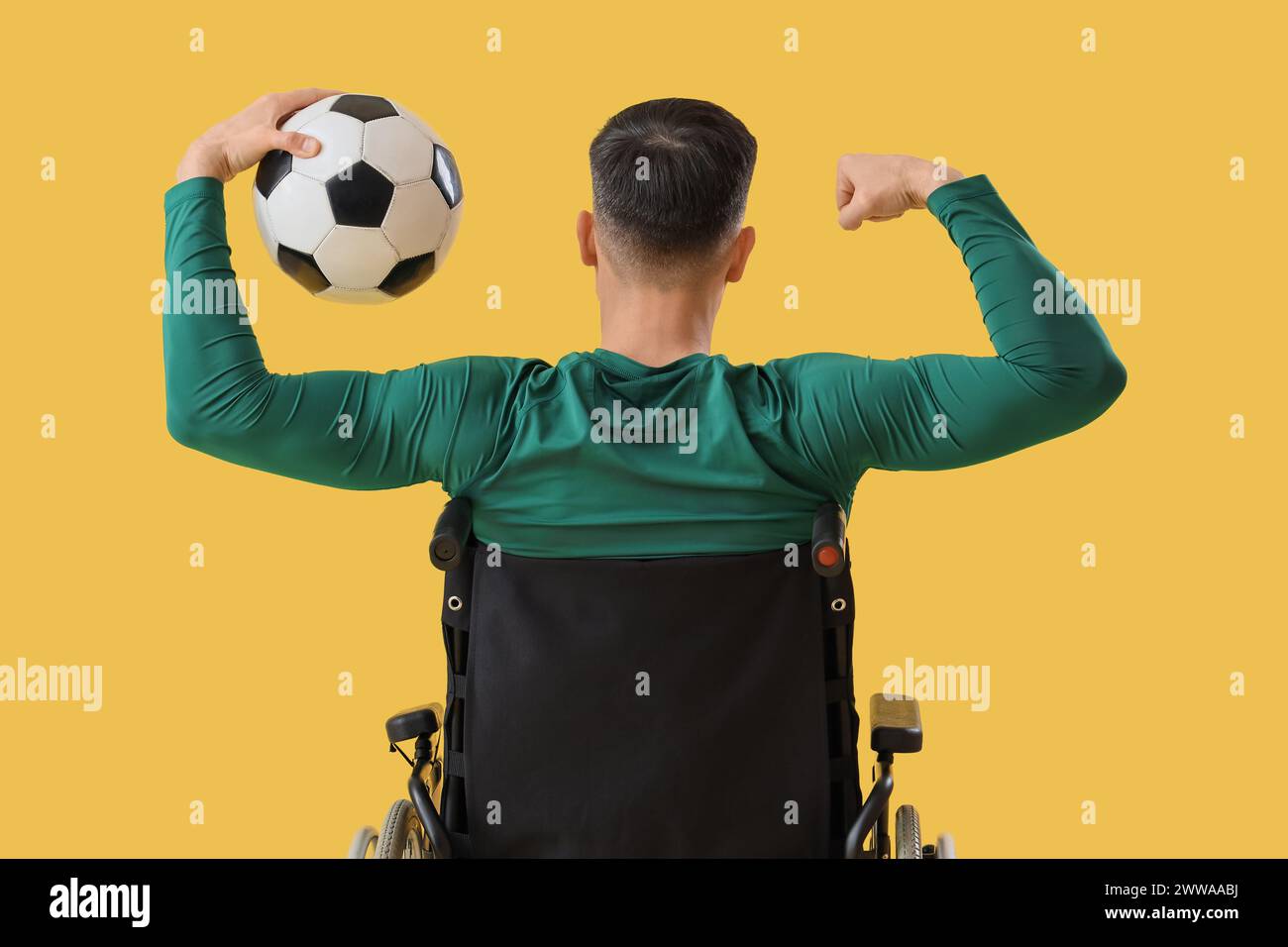 Male footballer in wheelchair with ball showing muscles on yellow ...