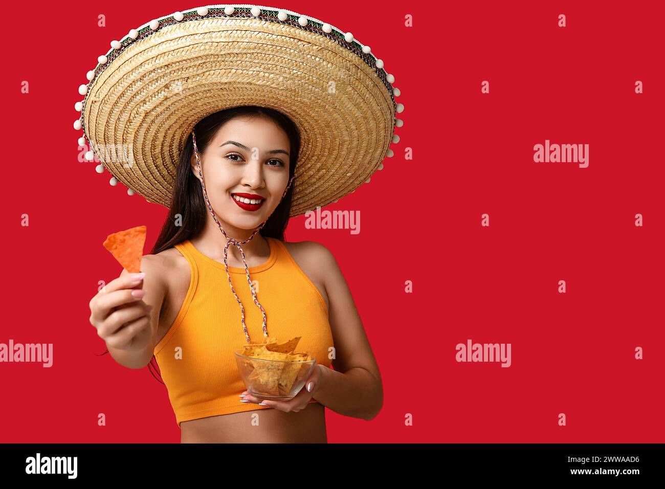 Portrait of young woman with sombrero and tortilla chips on red ...
