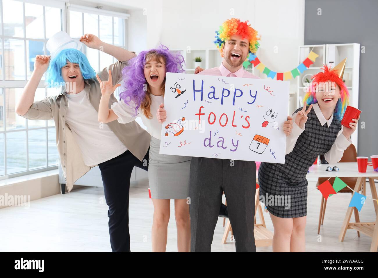 Business colleagues in funny wigs with poster celebrating April Fools ...