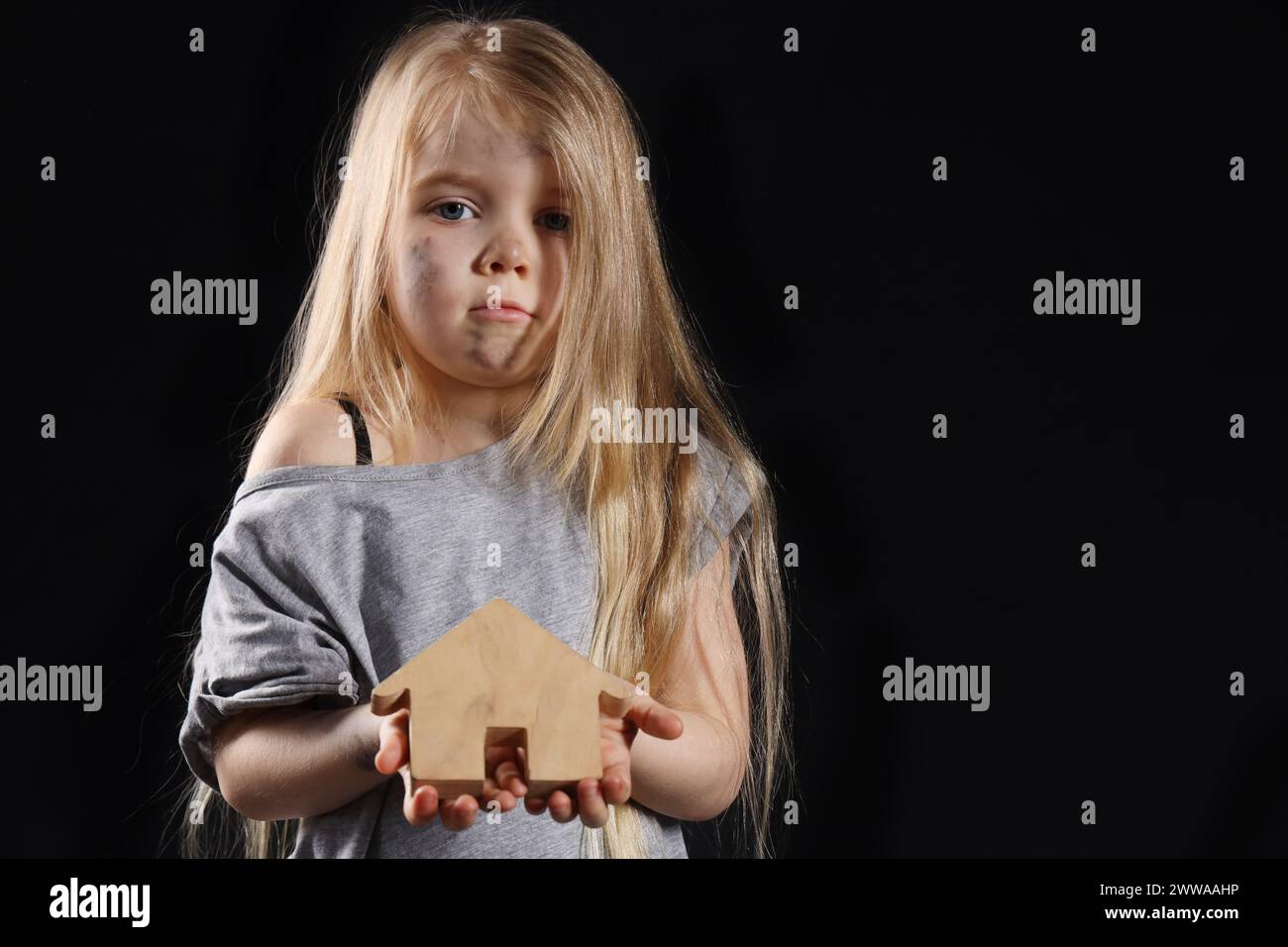 Homeless little girl with wooden figure of house on dark background ...