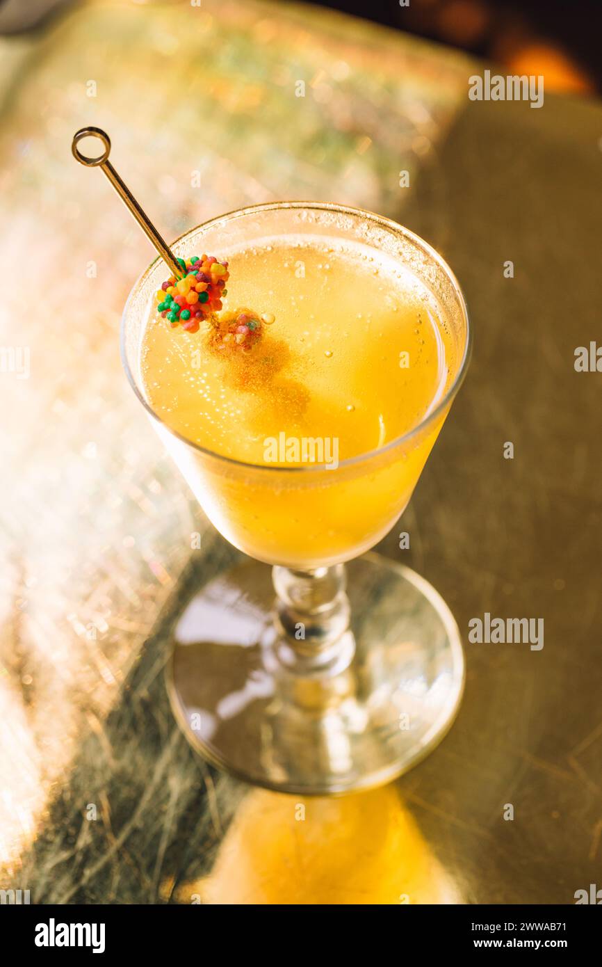 bubbly yellow cocktail with gummy cluster candy on cocktail pick ...