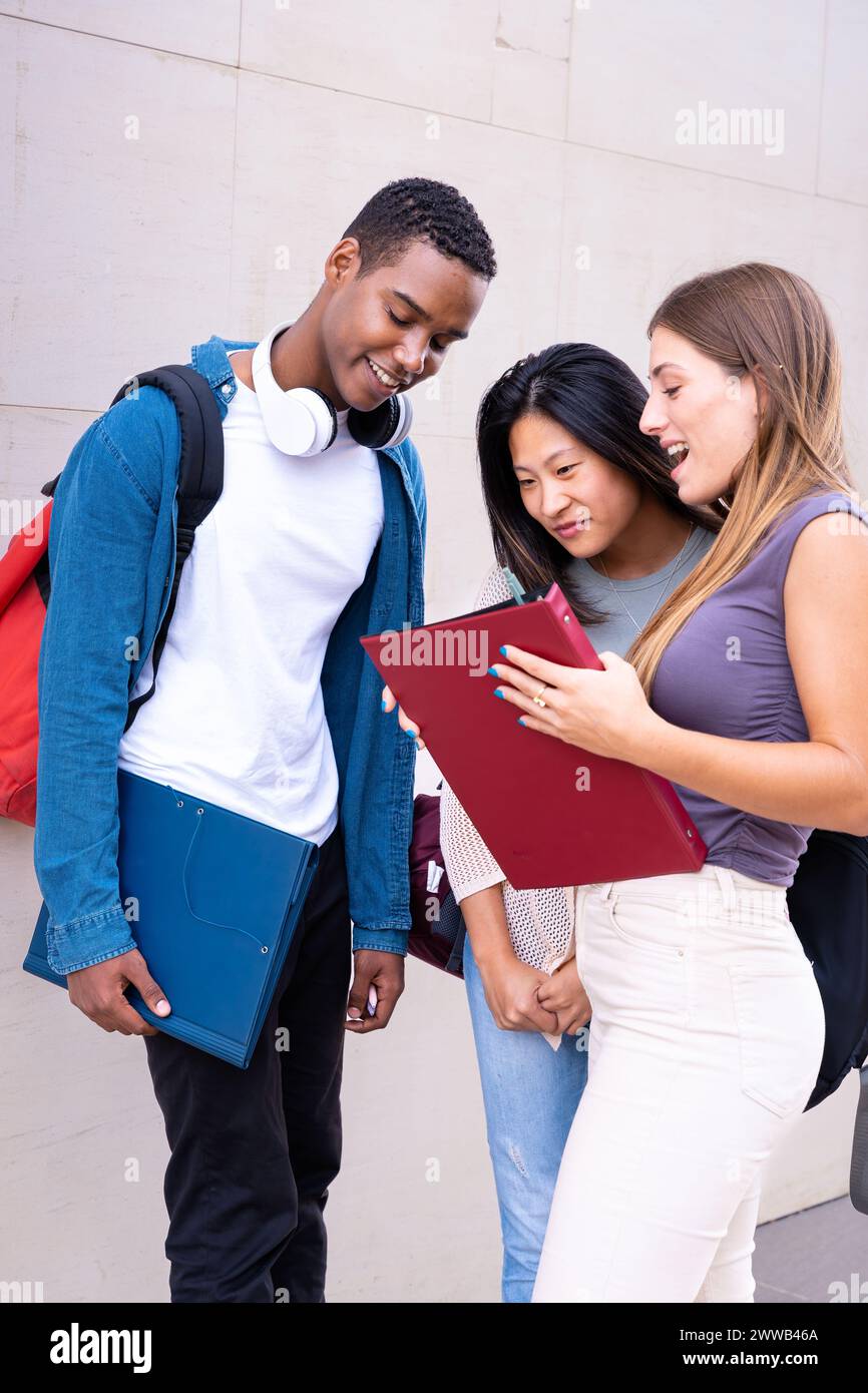 Smiling multiracial college student friends looking at notes, talking ...