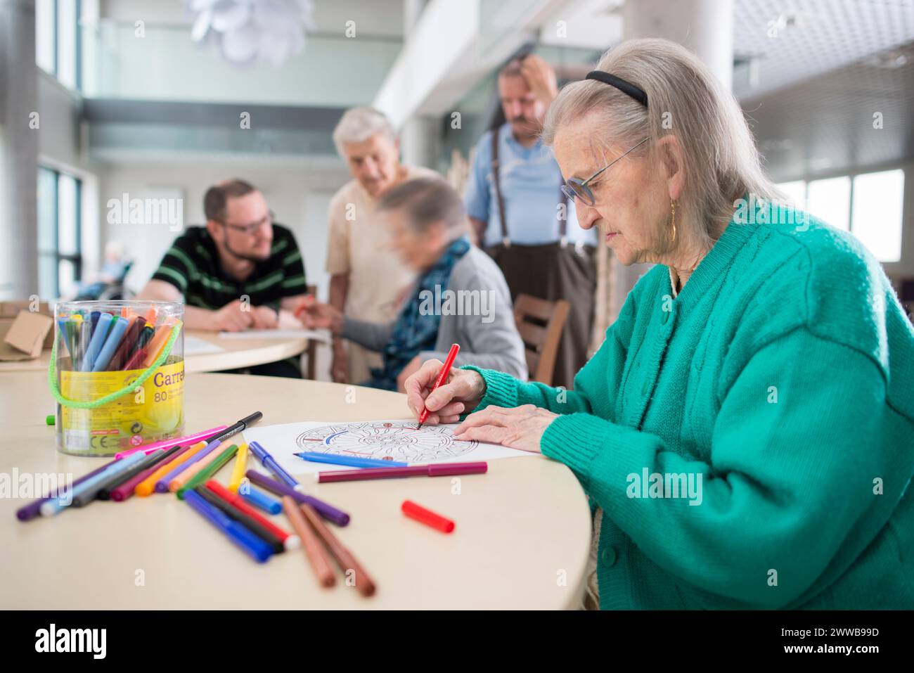 EHPAD - Resident drawing in a common room and animator helping another ...
