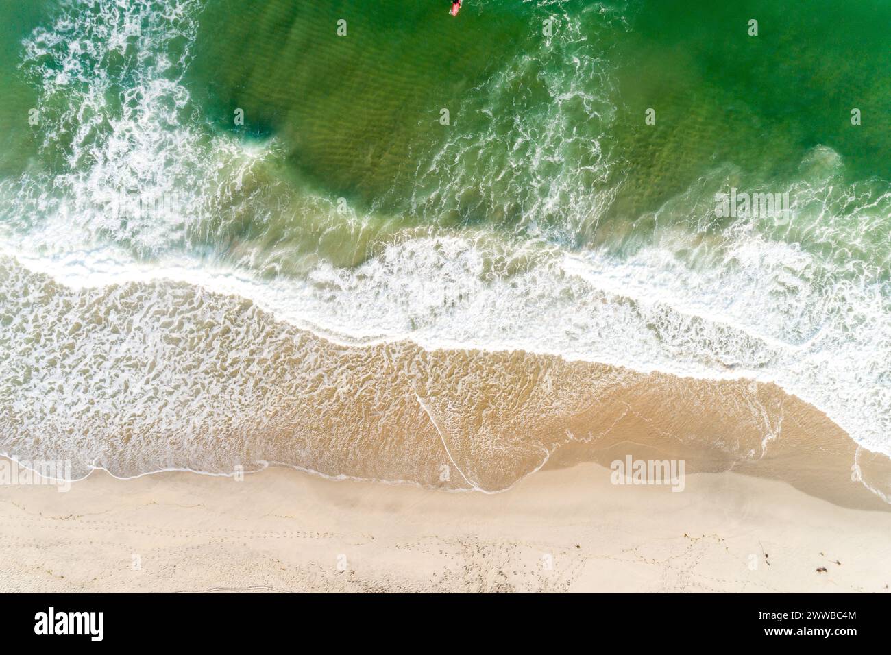 drone aerial overhead view of a surfer with a red surfboard in a beach ...