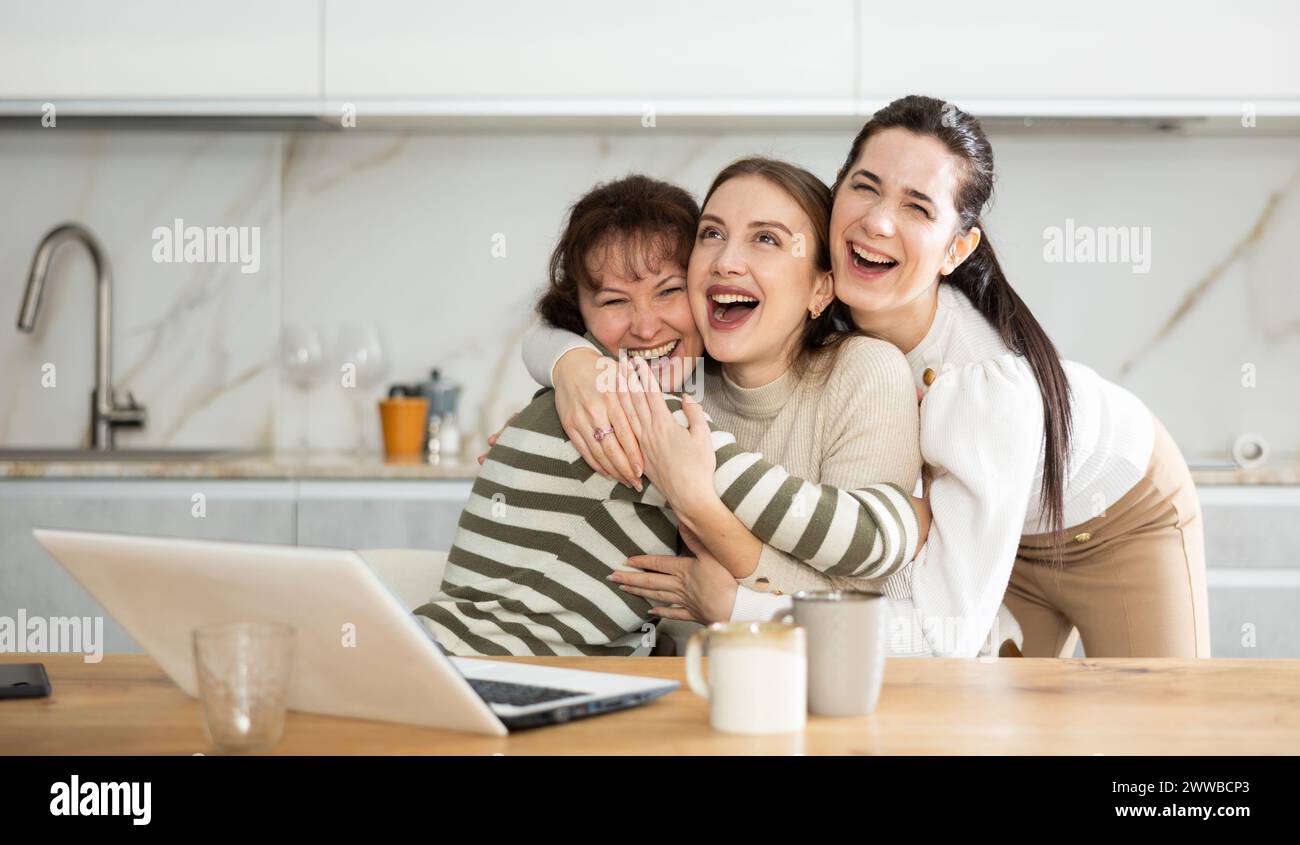 Three happy middle-aged woman expressing joy for winning in the kitchen ...