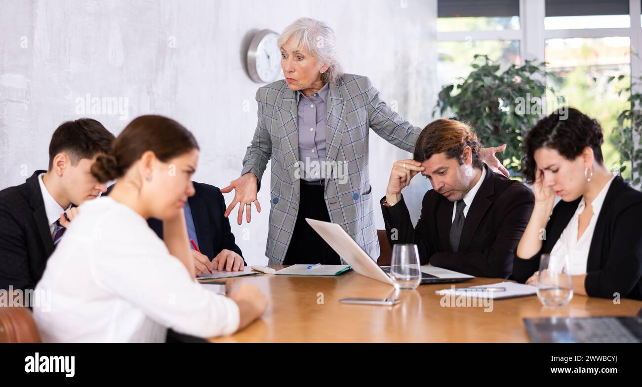 Outraged old female manager getting mad at office workers sitting with ...