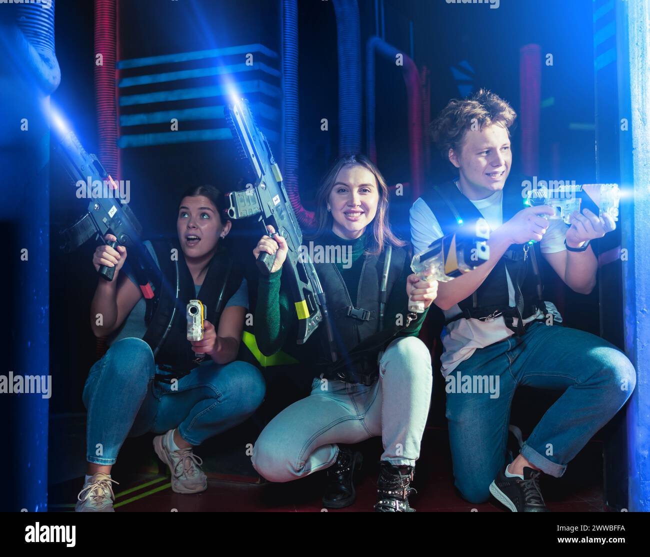 Modern young people with laser pistols playing laser tag on dark ...
