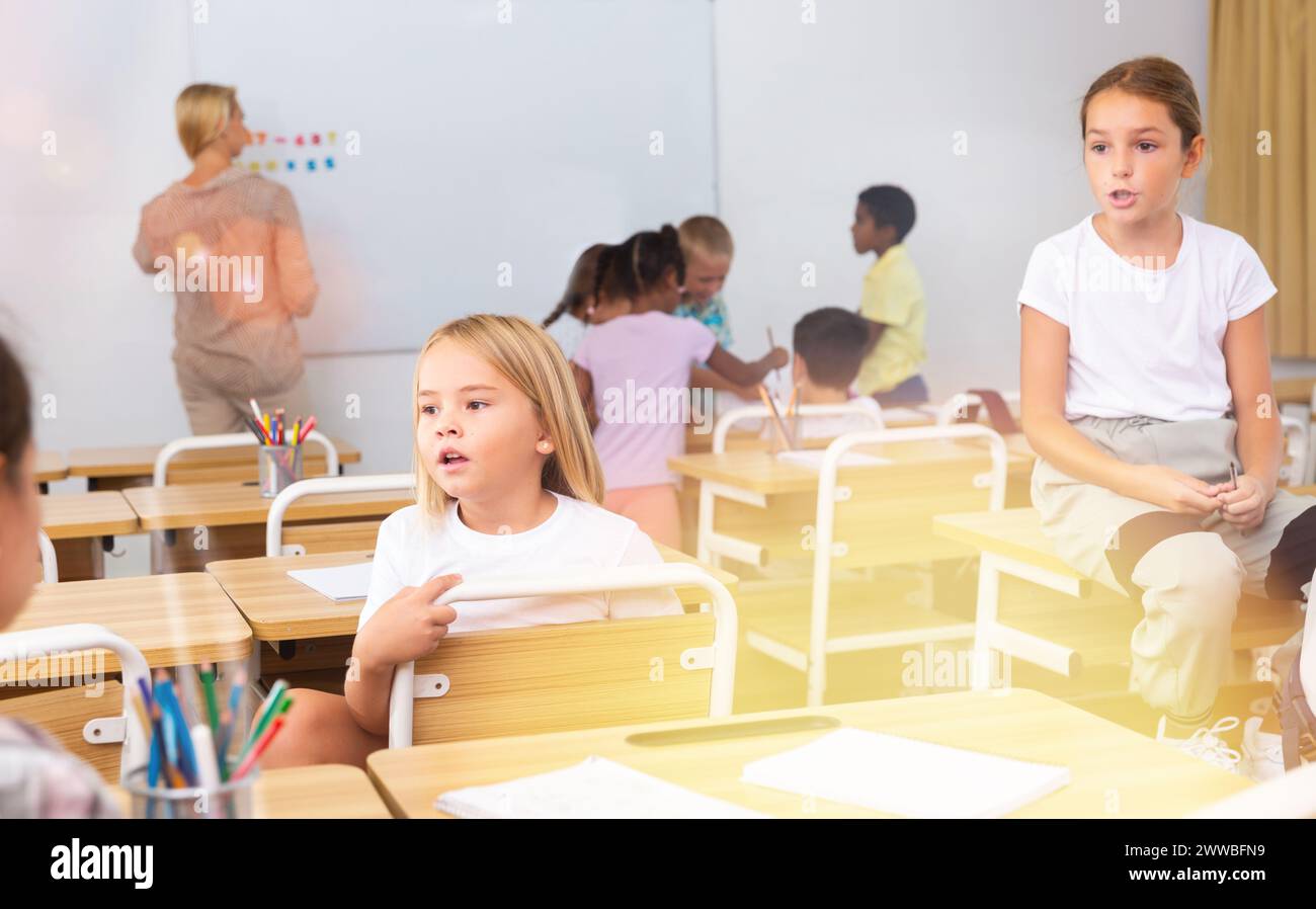 Positive primary school students are talking about homework at desk ...