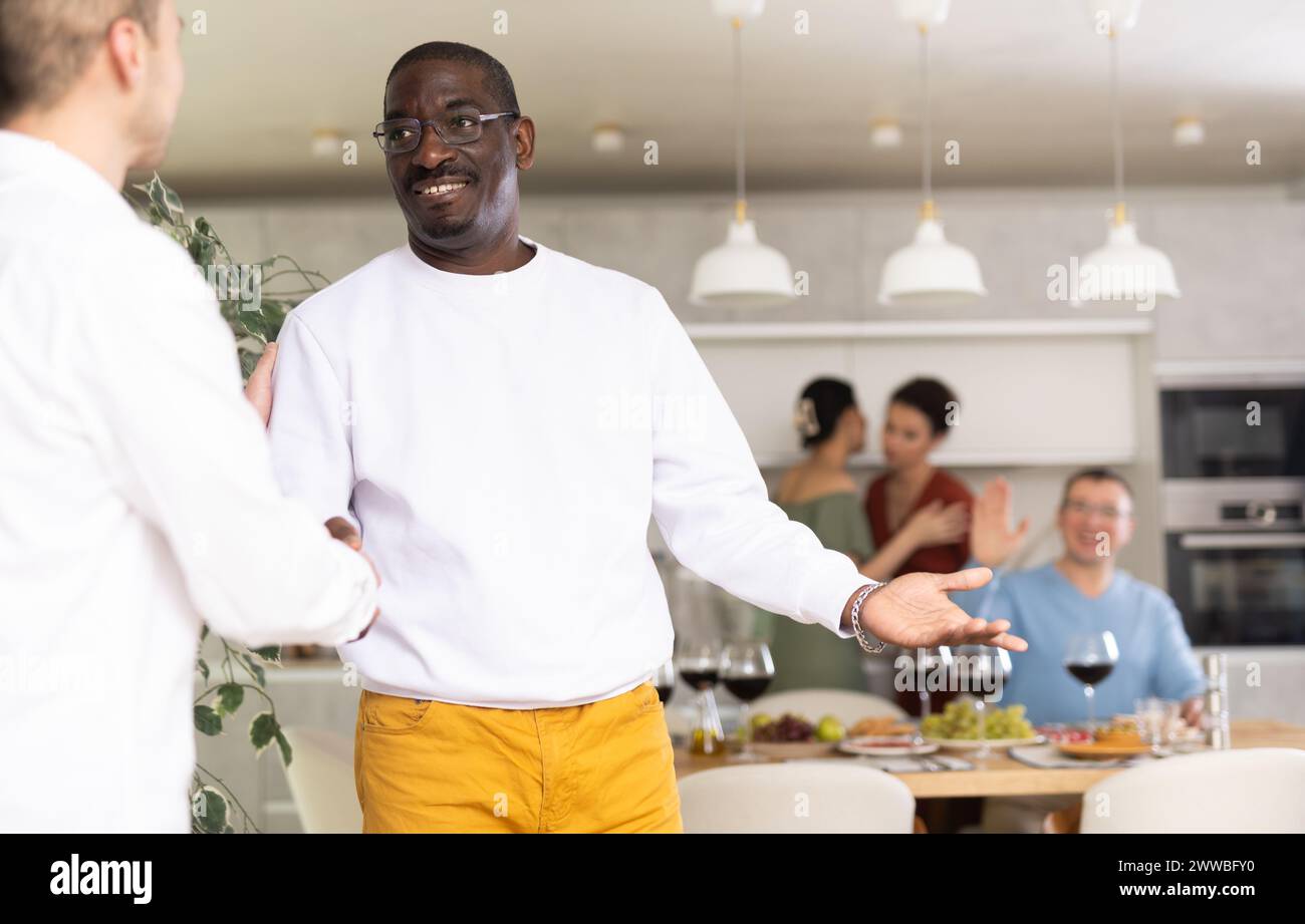 Smiling man welcoming friend to dinner party with handshake Stock Photo ...