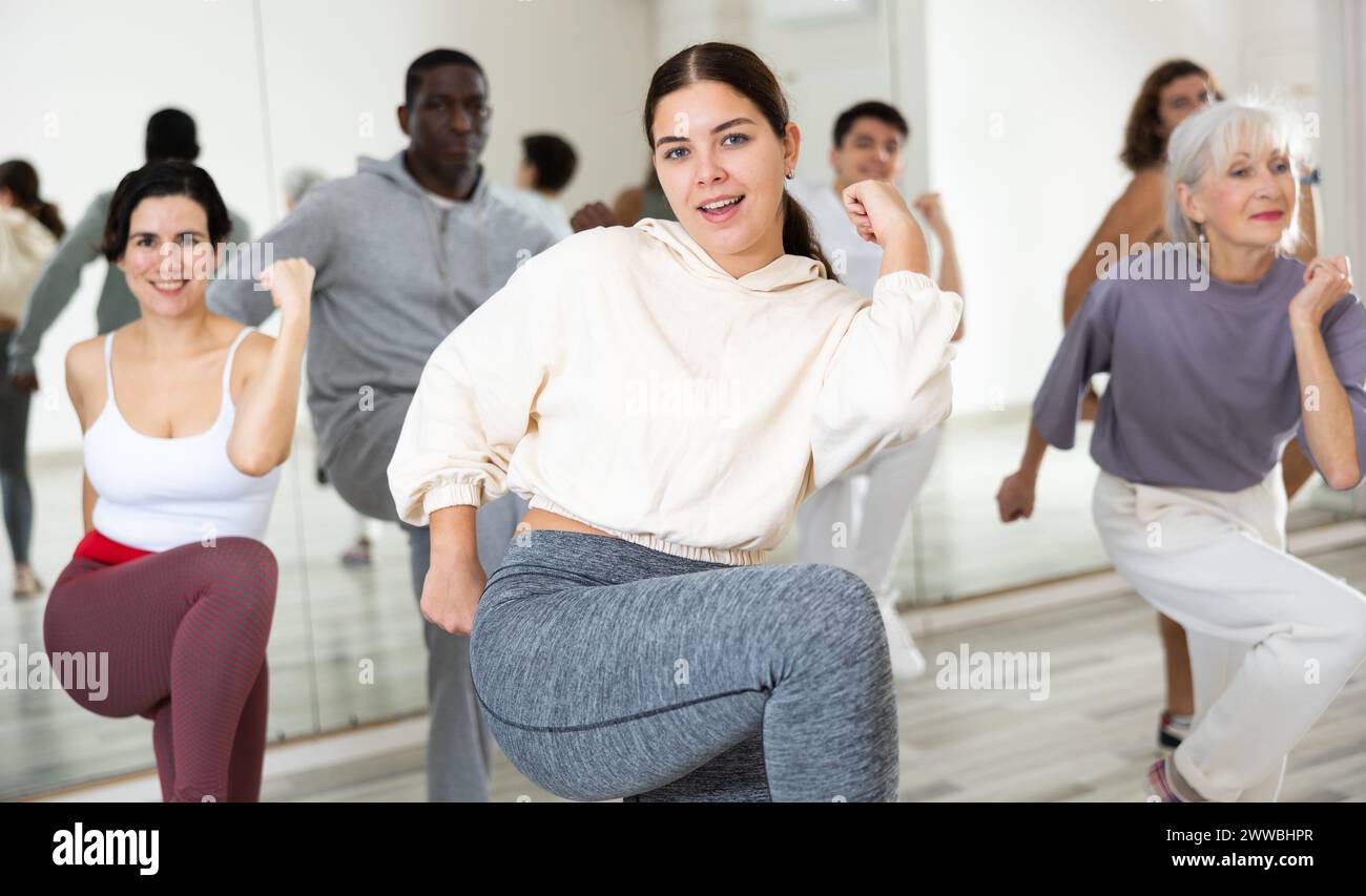 Cheerful young lady learning new modern dance in group dance lesson ...