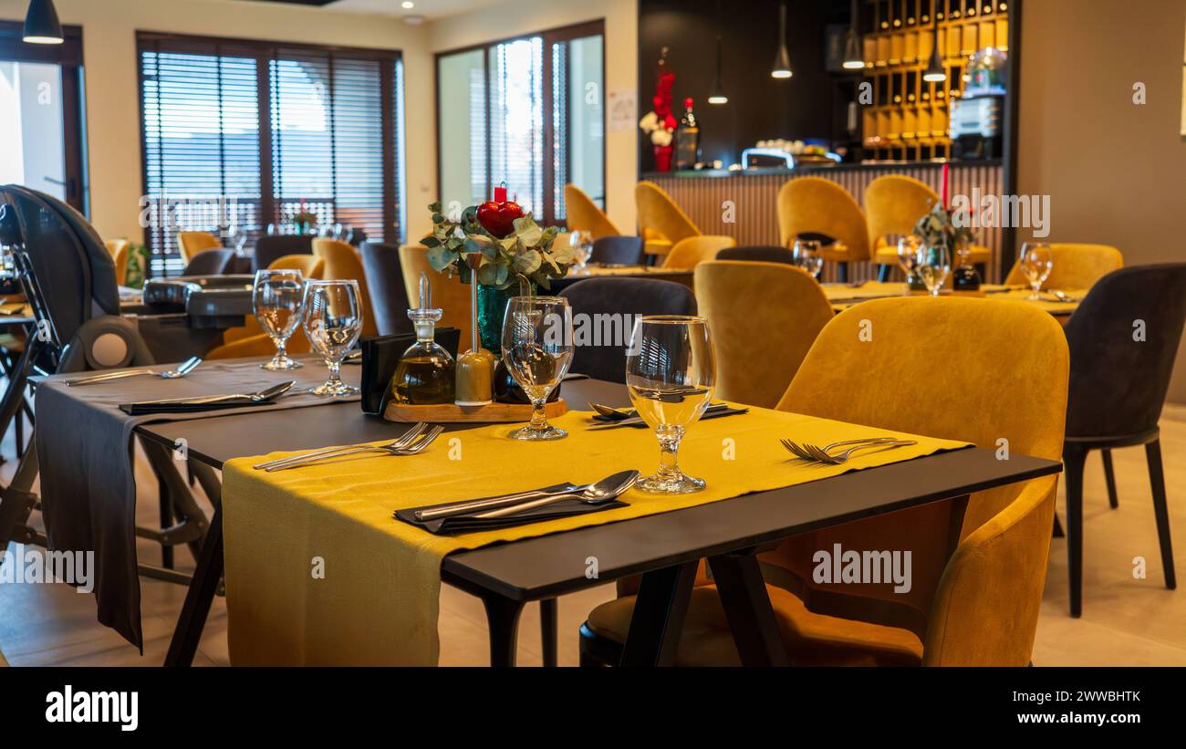 A restaurant scene with yellow tablecloths, glassware, and cutlery ...