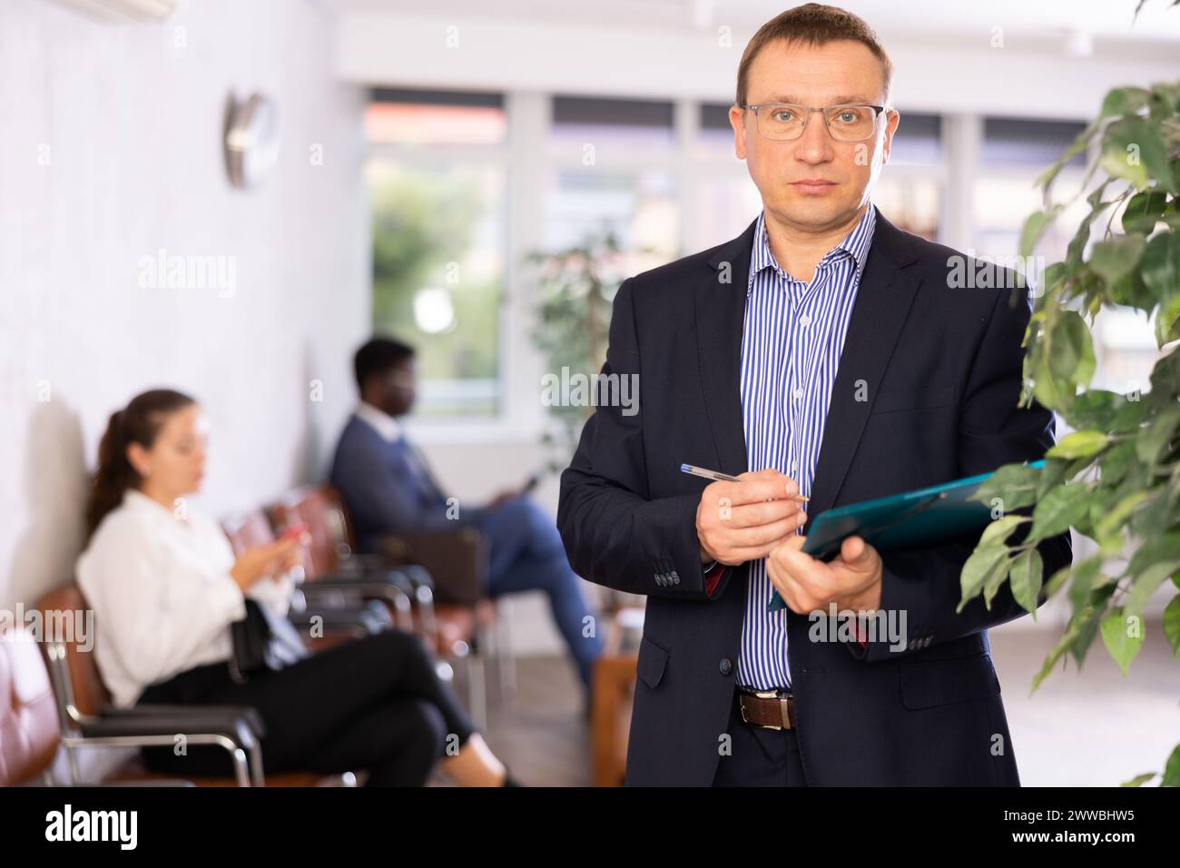 Dispassionate secretary man stands at reception with folder and list of ...
