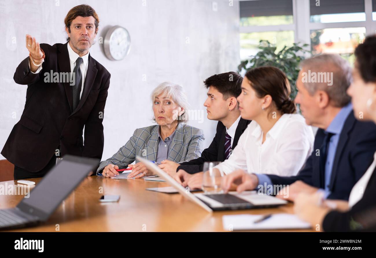 Dissatisfied male boss telling off office workers of different ages ...