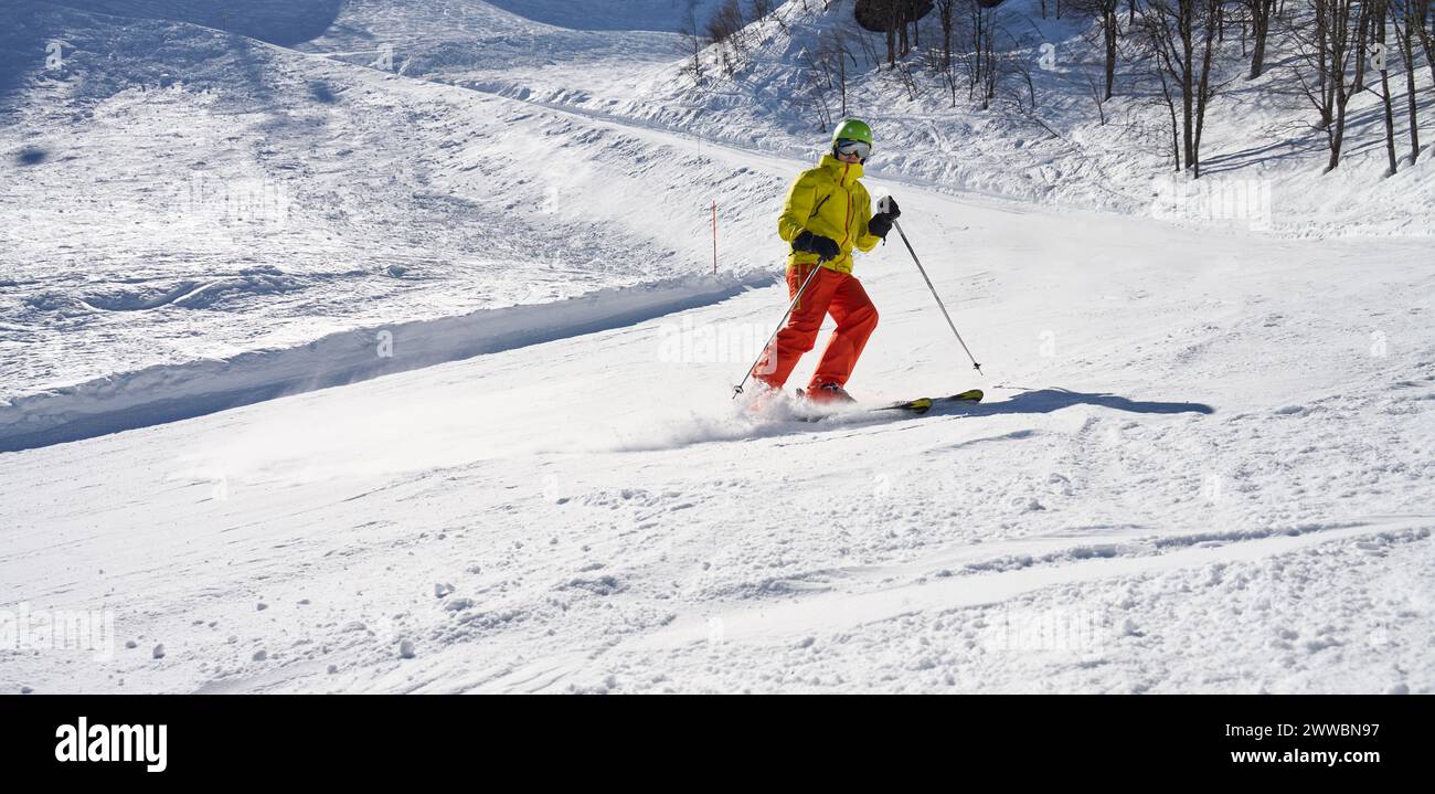 Skier in motion, carving turns on a snowy ski slope under blue skies ...