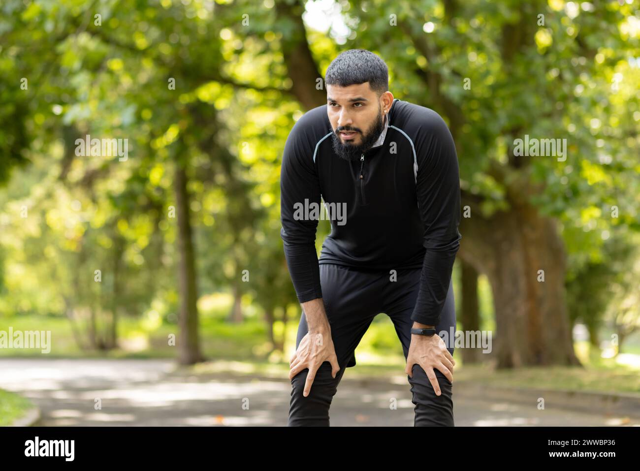An athletic man pauses for rest after a run, hands on knees, in a ...