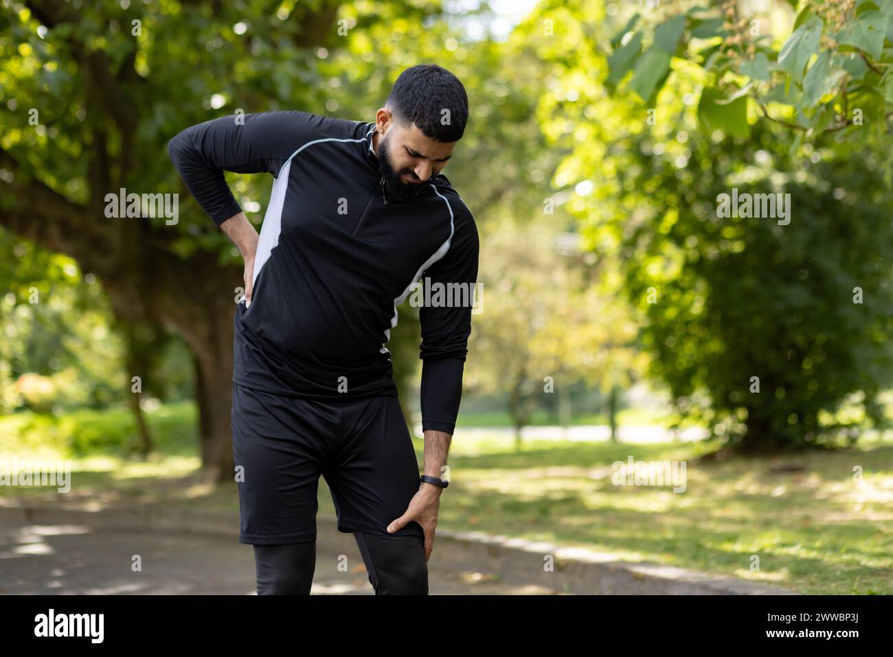 An athletic man in sportswear holds his lower back in pain while ...