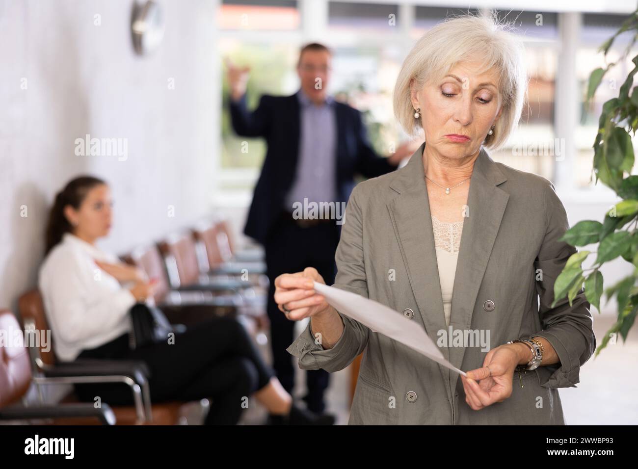 Upset old woman standing in waiting room with her back to person who is ...