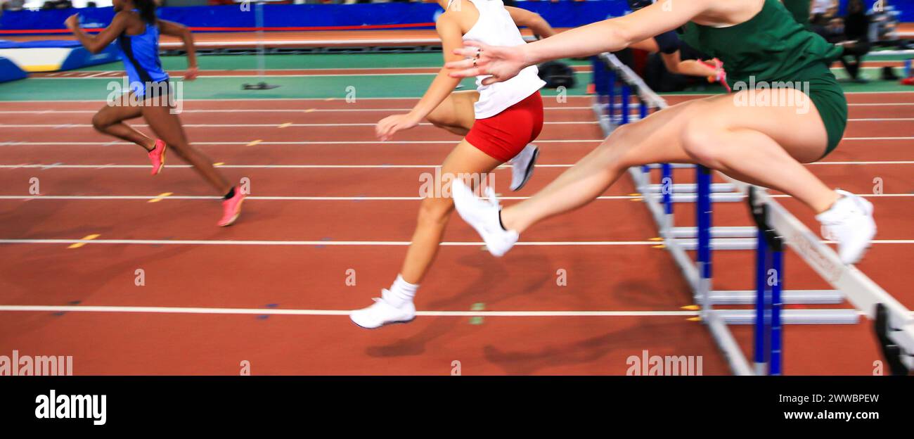 Side view of high school girls running over hurdles while racing ...