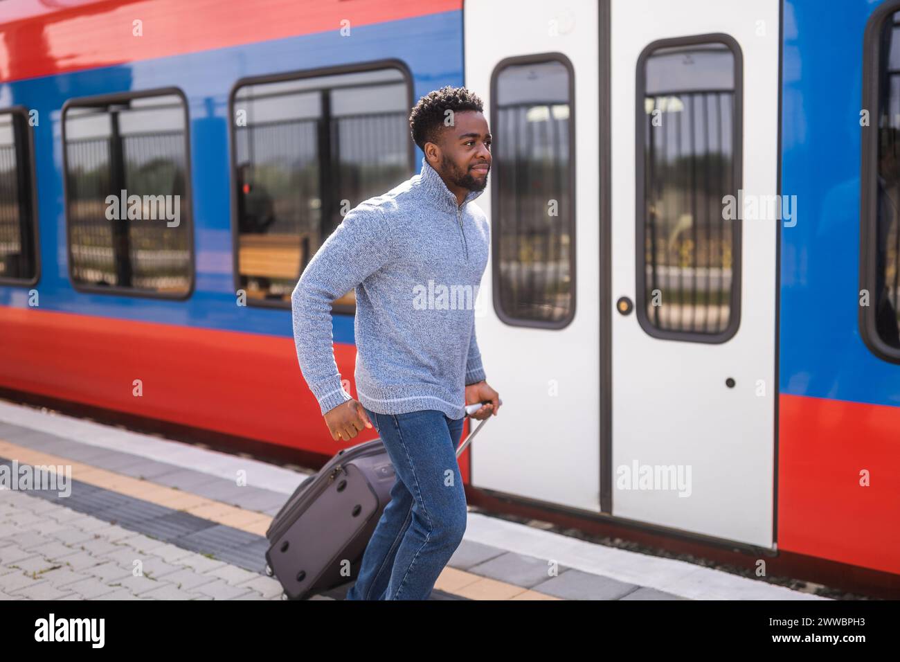 Man running to a leaving train along railway station with suitcase ...