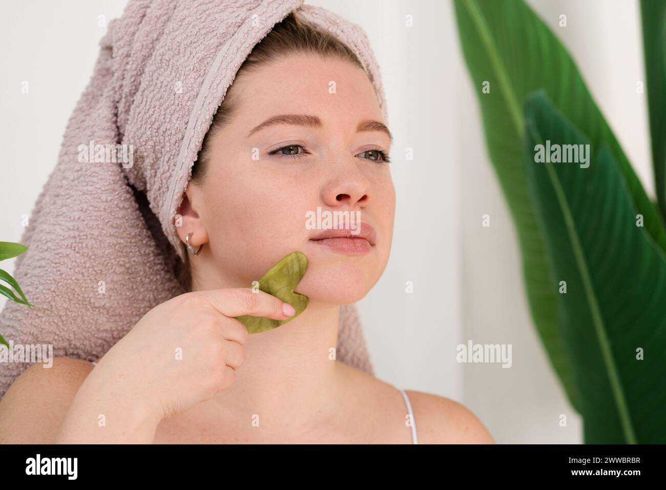 Woman performing facial massage with gua sha stone scraper. Young woman ...