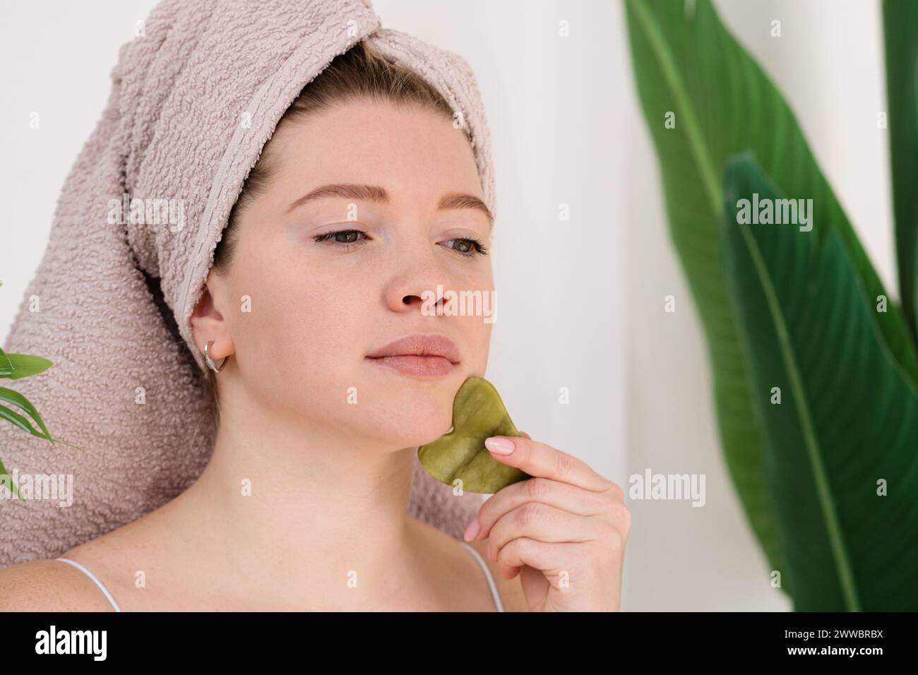 Woman performing facial massage with gua sha stone scraper. Daily self ...