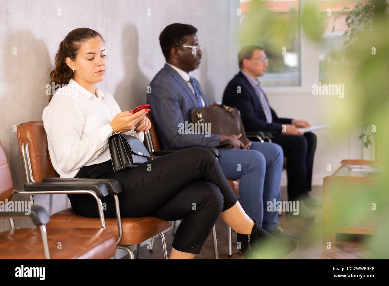 Young woman sitting in line at reception with phone Stock Photo - Alamy