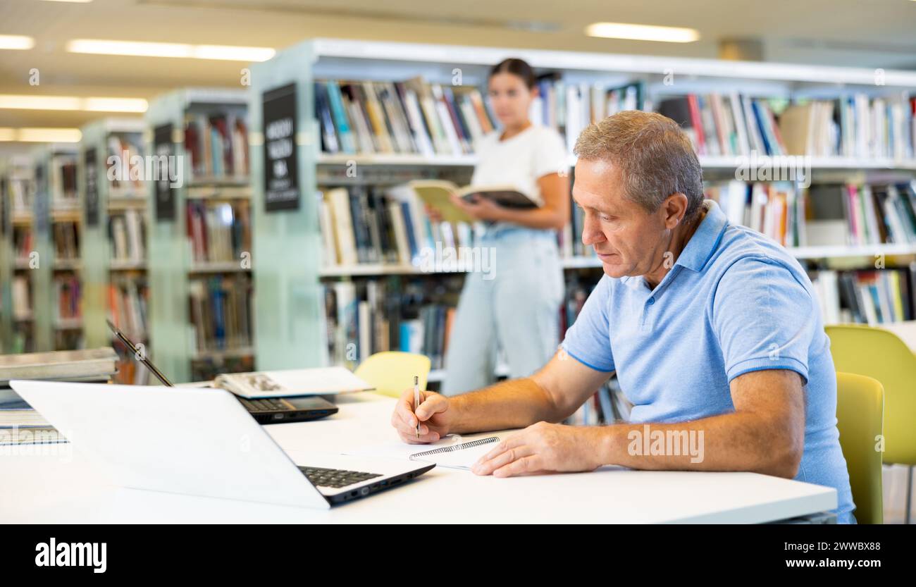 Concentrated elderly man writing in planner while searching info in ...