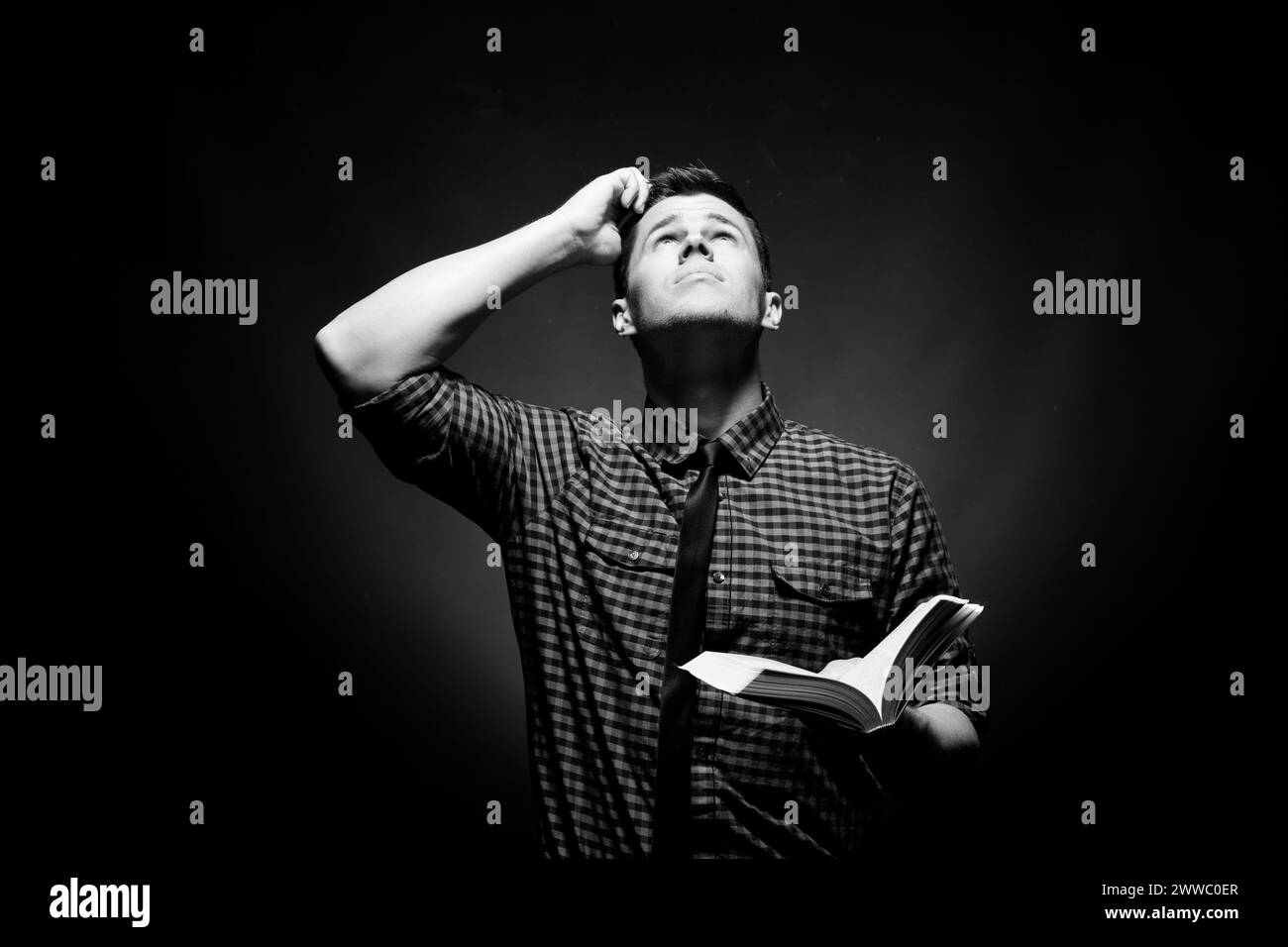 A well dressed man holding a Bible and looking up at God in confusion ...