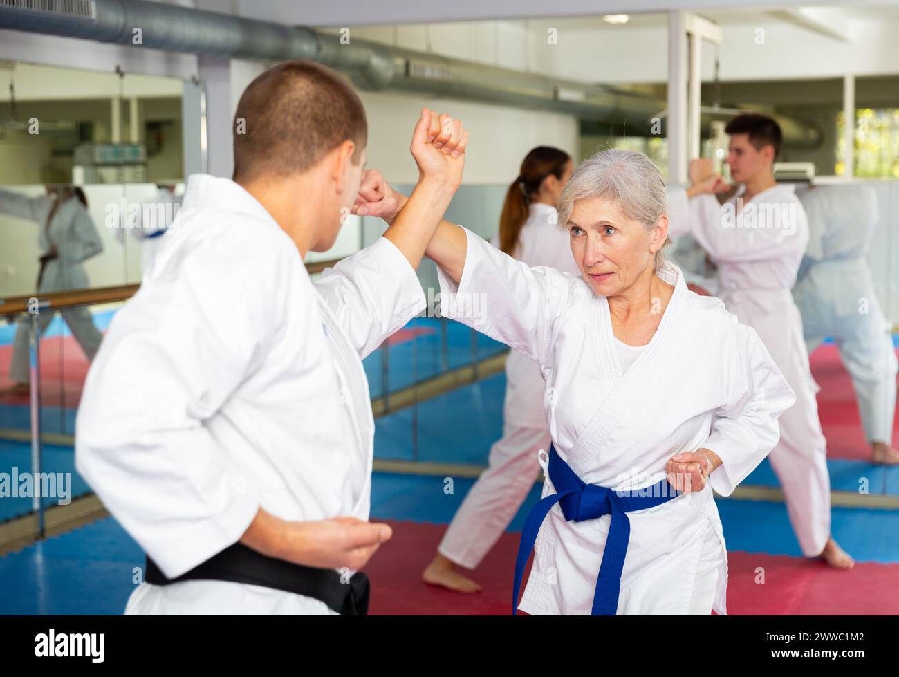 Portrait of woman wearing white kimono sparring with male opponent during martial arts training ...