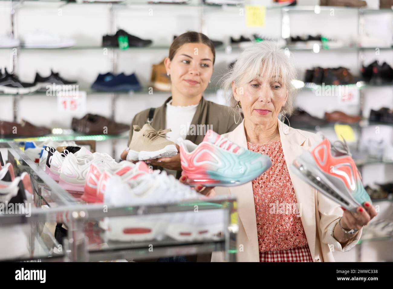 Two positive women of different ages choose new sneakers together in ...