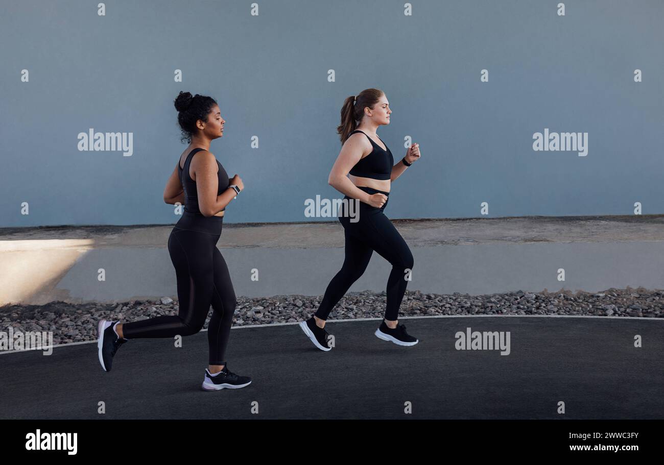 Two women with different body types running outdoors. Side view of two ...