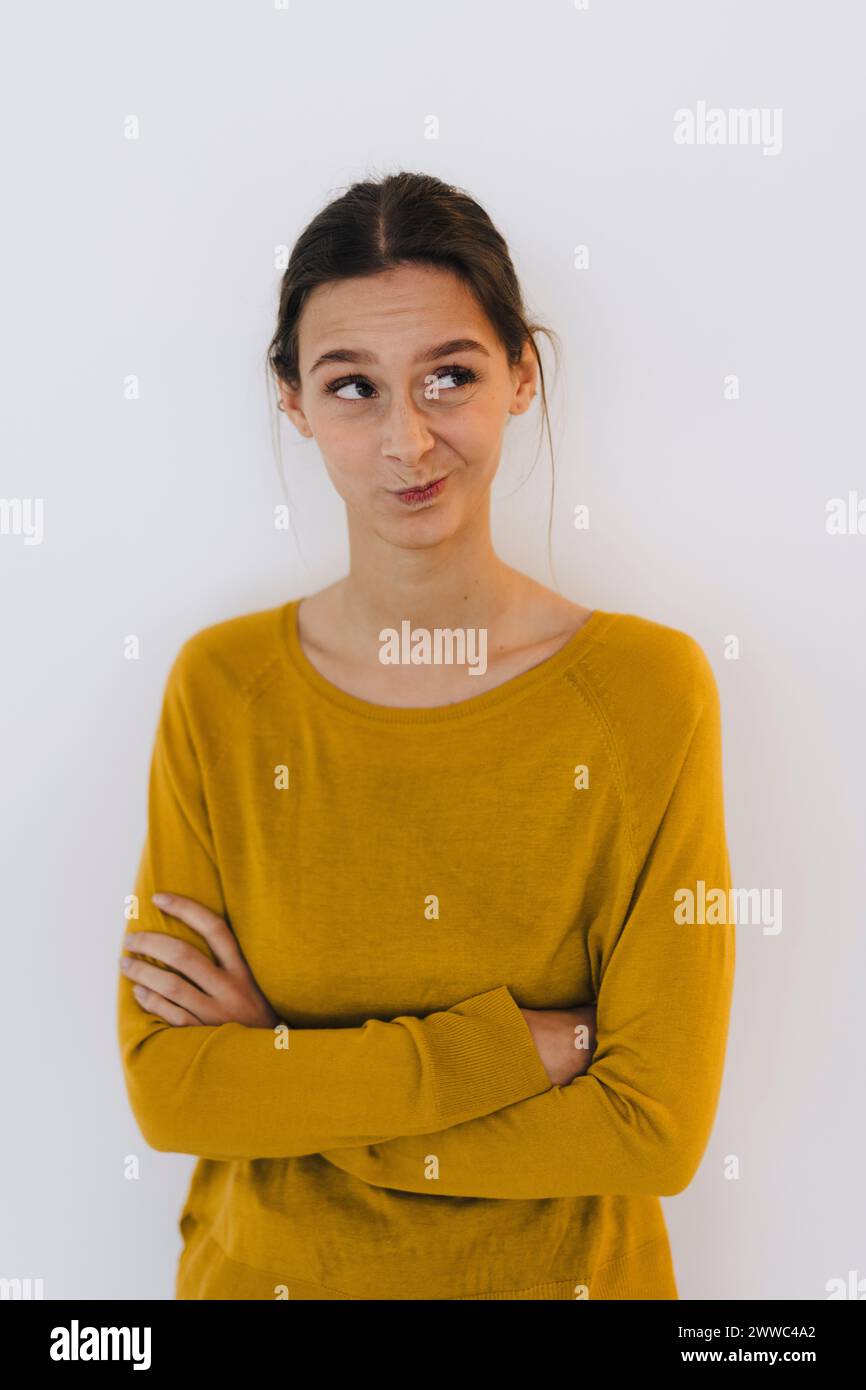 Young businesswoman standing with arms crossed and making face in front ...