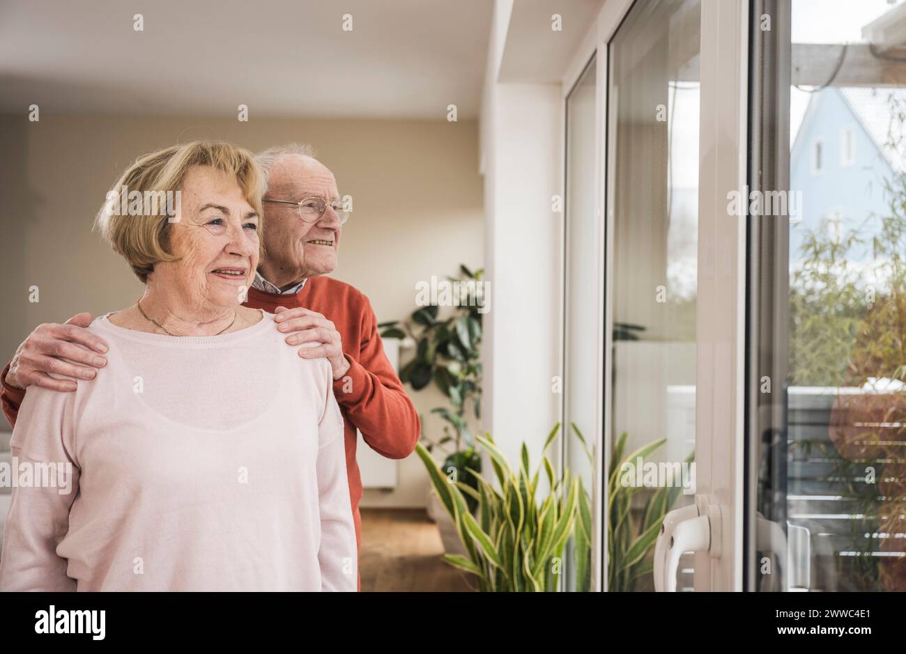 Happy senior man and senior woman looking through window at home Stock ...