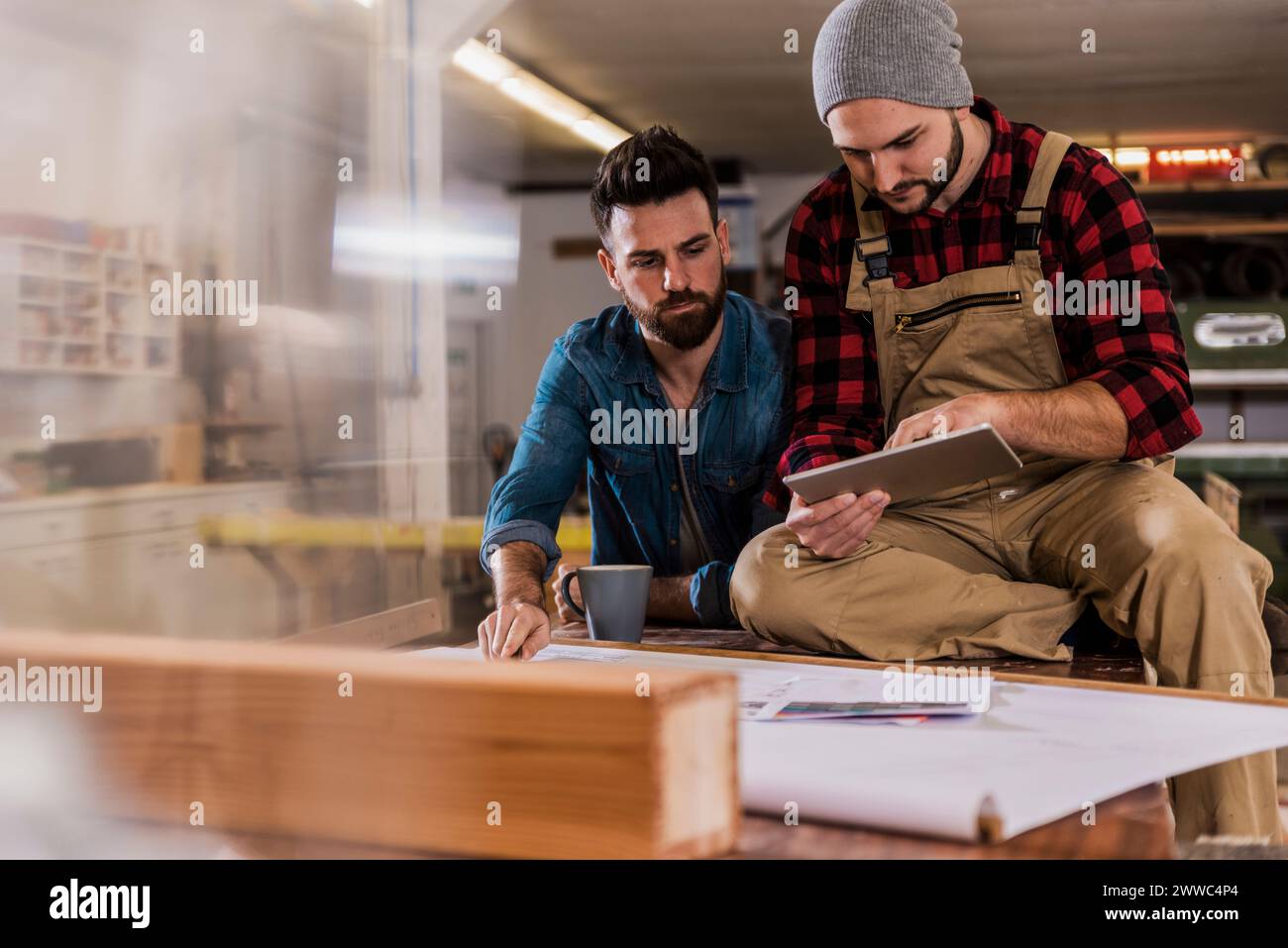Carpenter sharing tablet PC with colleague sitting on workbench at workshop Stock Photo - Alamy