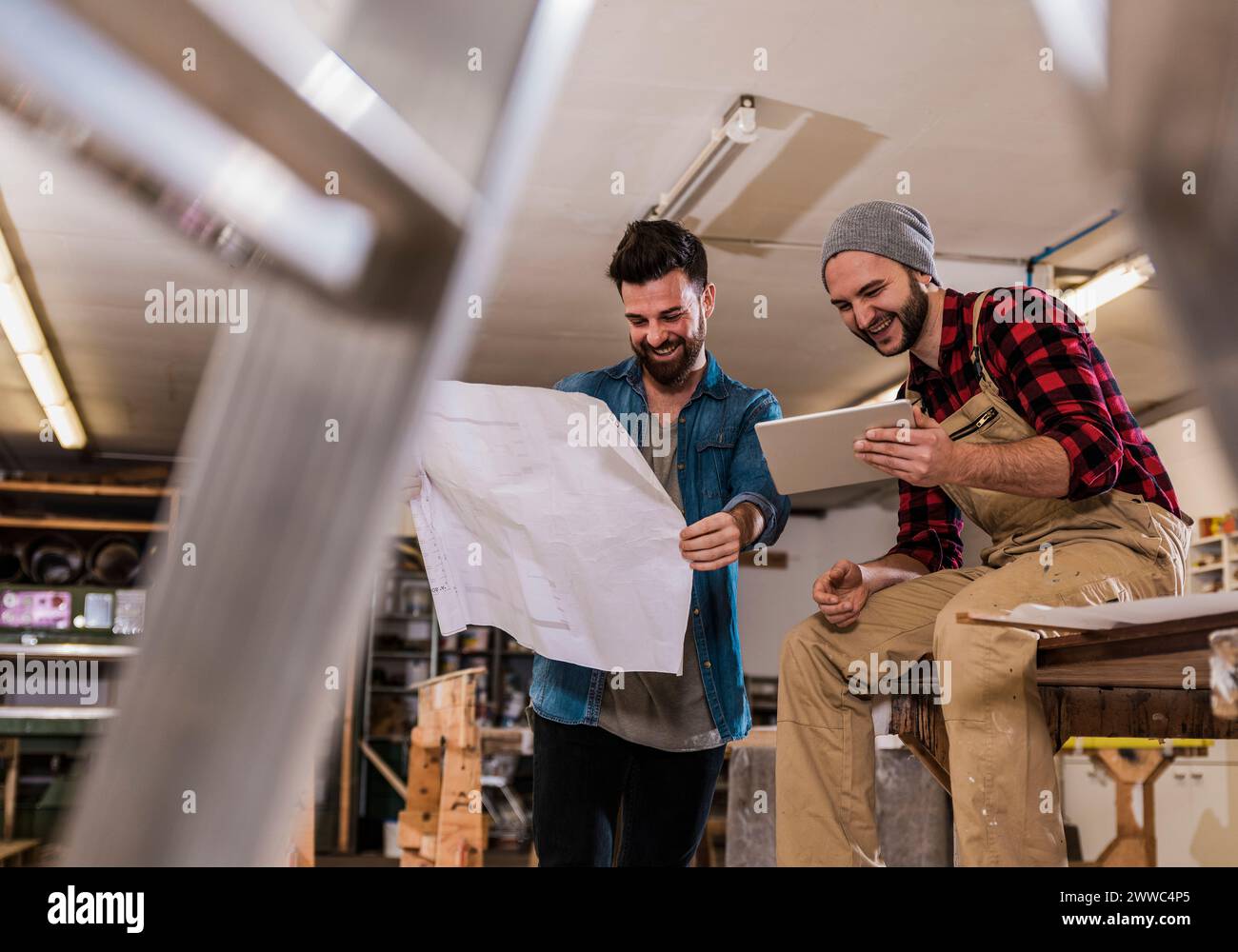 Happy craftsmen examining blueprint through tablet PC at workshop Stock ...