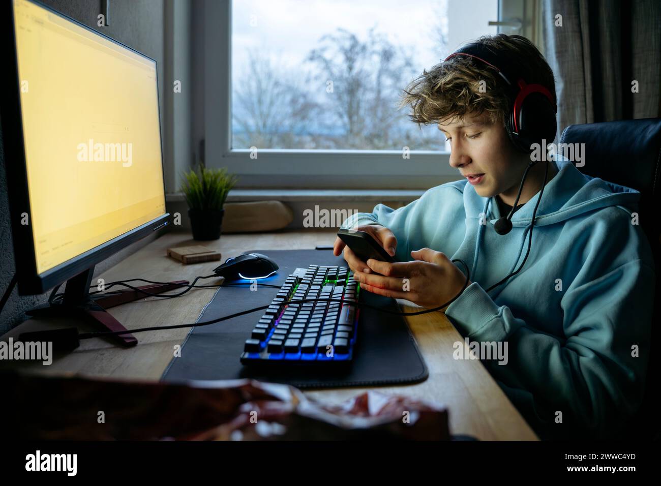 Teenage boy sitting near computer and using smart phone at home Stock ...