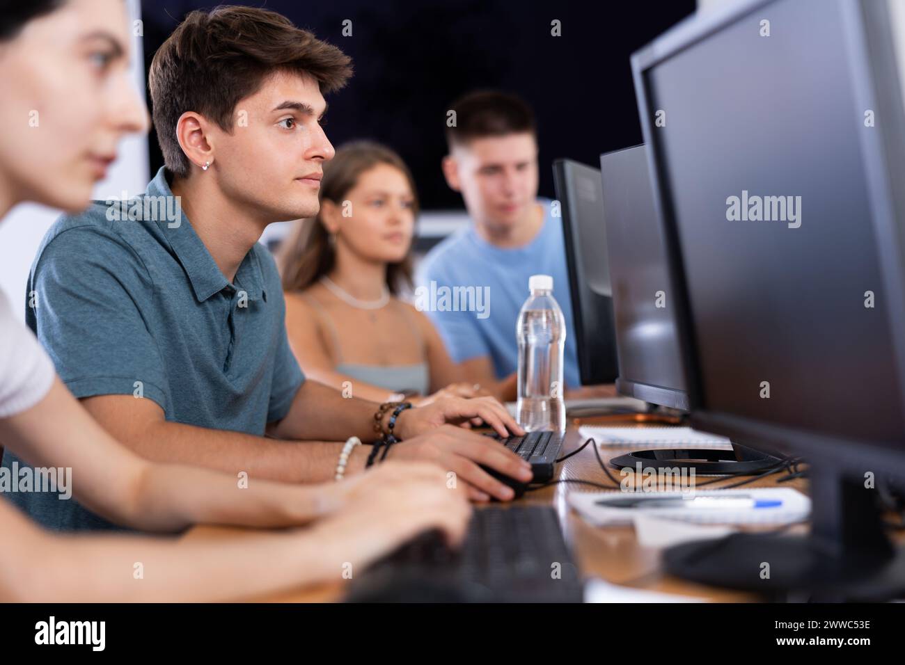 Guy student of computer courses looks at monitor screen, types on ...