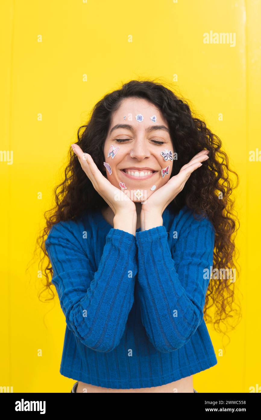 Happy woman smiling with stickers on face against yellow background ...