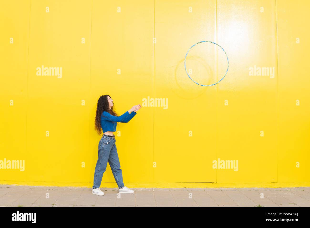 Woman throwing hula hoop standing against yellow background Stock Photo ...