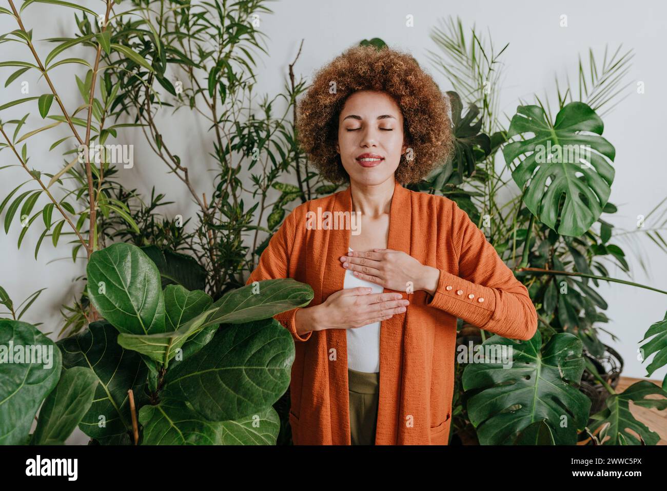 Smiling woman breathing with hands on chest near plants Stock Photo - Alamy