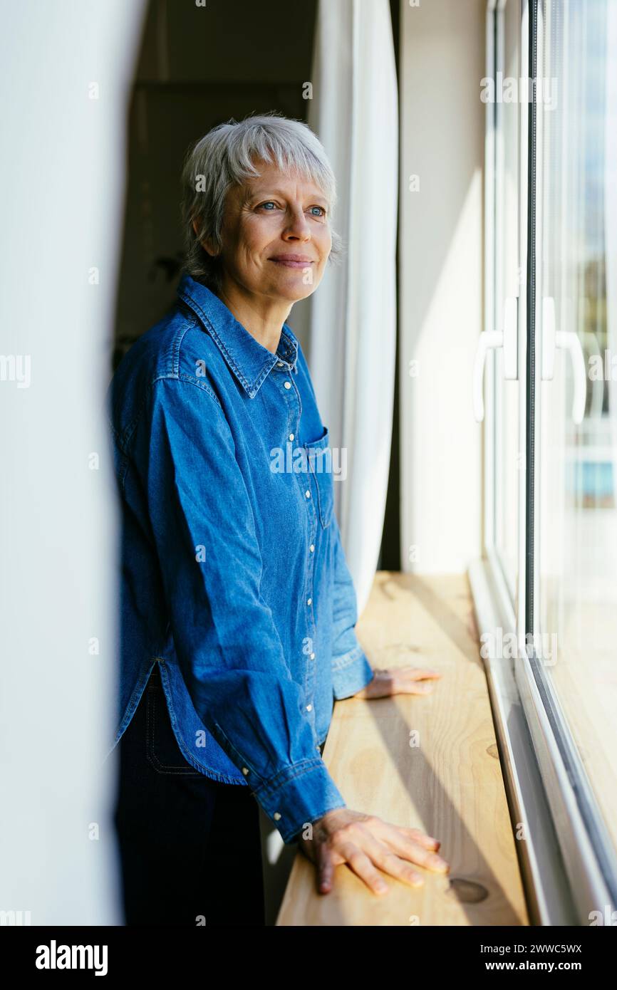 Mature woman standing and looking out of window at home Stock Photo - Alamy