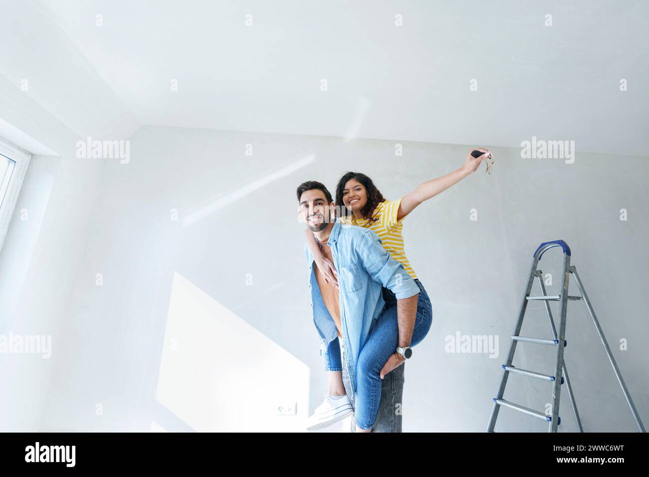 Happy man giving piggyback ride to girlfriend holding house key at new ...