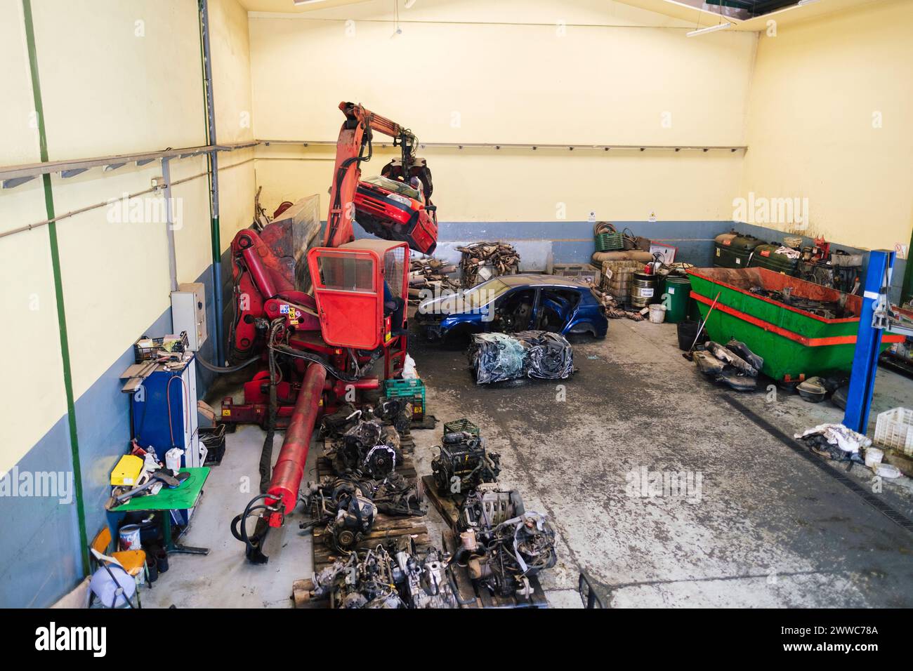 Mechanic operating crane machine to carry scrap vehicles at workshop ...