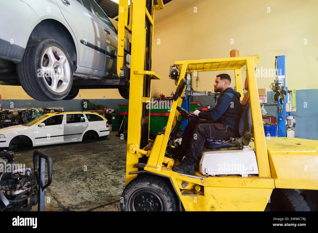 Mechanic operating forklift and lifting car at workshop Stock Photo - Alamy