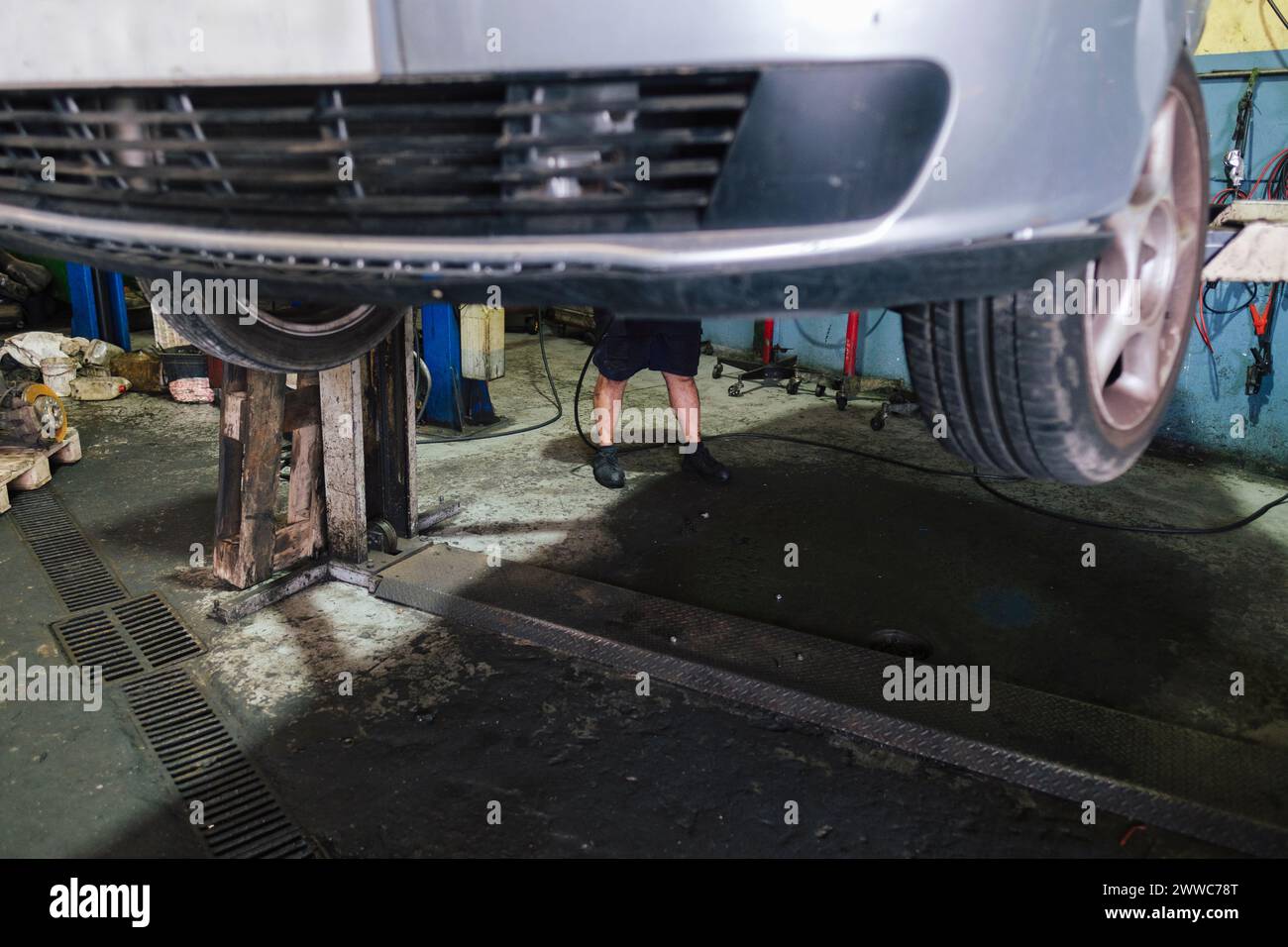 Mechanic working behind lifted vehicle at workshop Stock Photo - Alamy