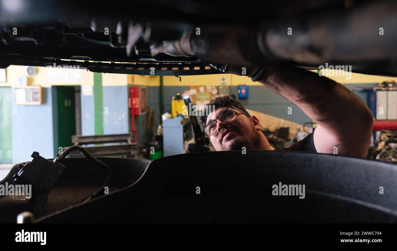 Mechanic using flashlight and inspecting lifted vehicle at workshop ...
