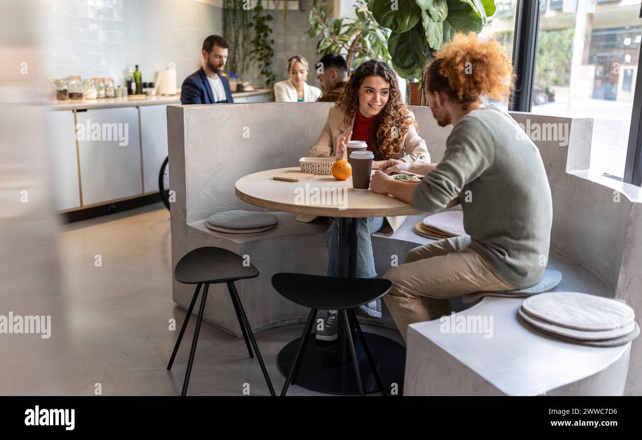 Business colleagues having lunch sitting on seat at office cafe Stock ...