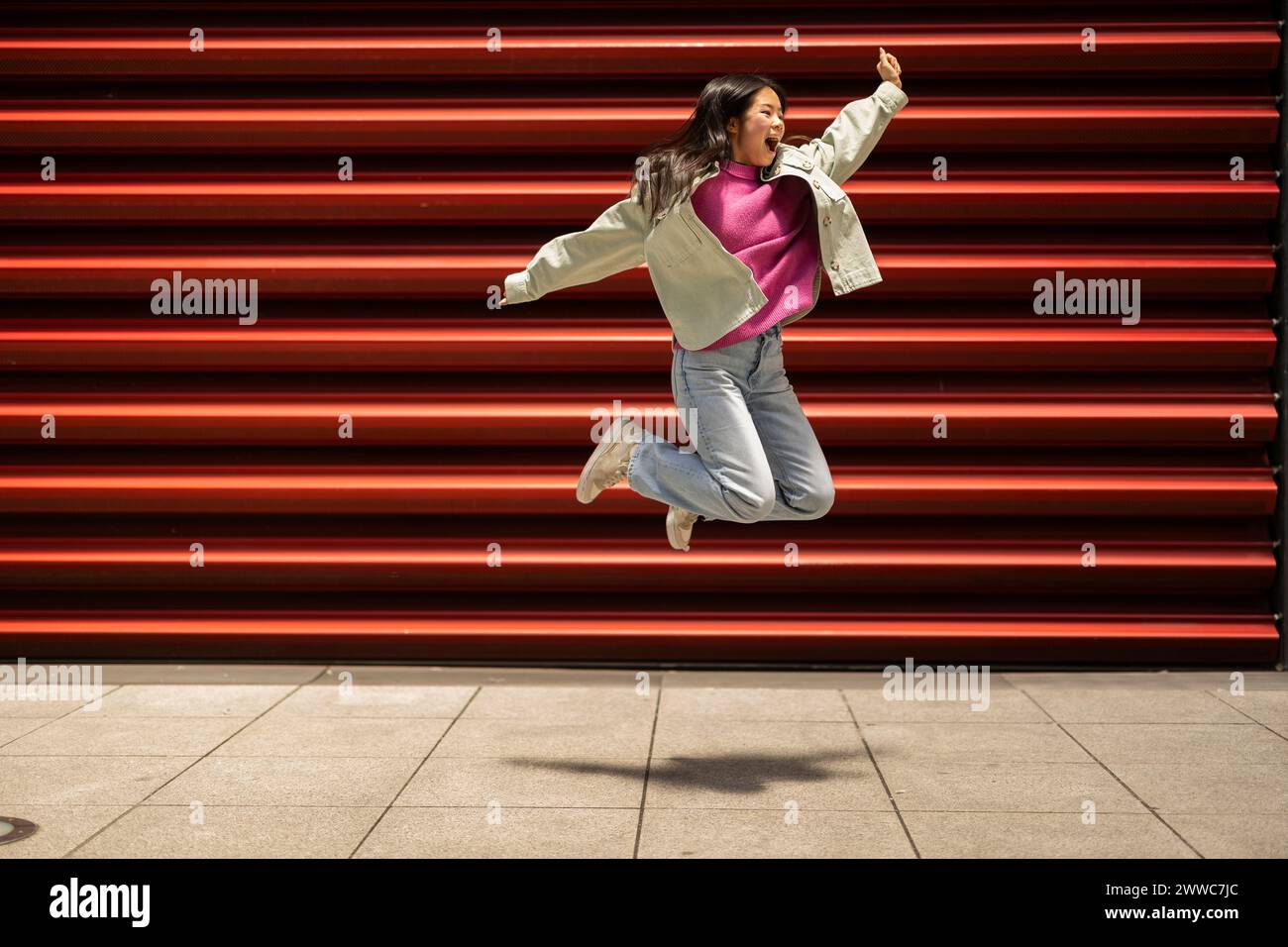 Happy young woman jumping in front of shutter Stock Photo - Alamy