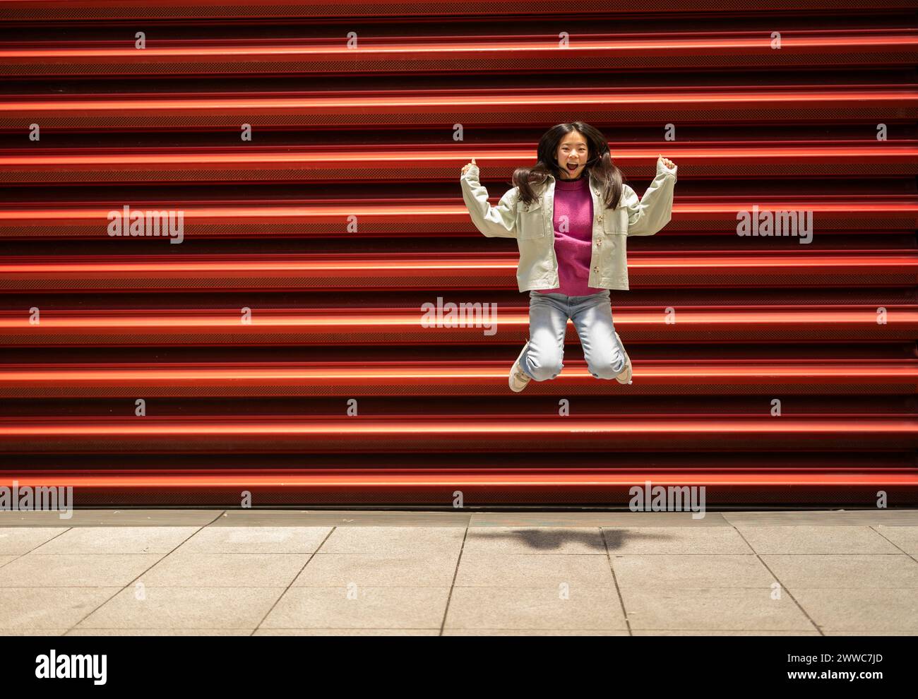 Cheerful young woman jumping in front of shutter Stock Photo - Alamy