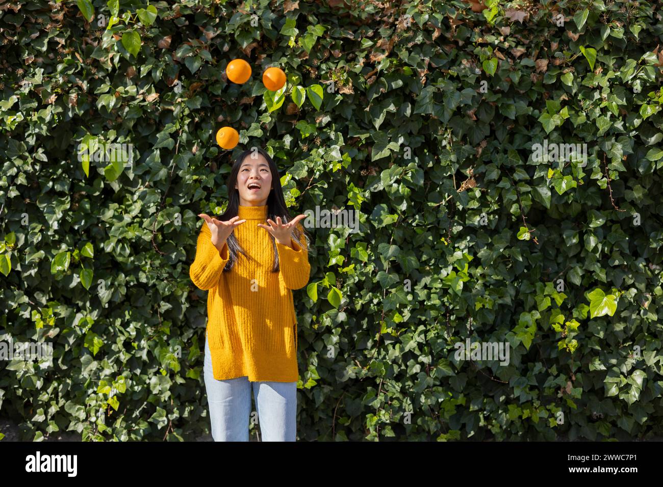 Happy young woman juggling oranges in front of plants Stock Photo - Alamy